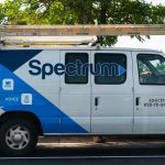 A parked van used by a Spectrum cable technician. The van has the Spectrum logo on its side and a ladder stowed on the roof.