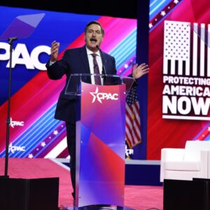 Mike Lindell speaks on stage at the Conservative Political Action Conference, flanked by signs that say "CPAC" and "Protecting American now."