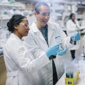 Doctors examining test tubes while coworker working in background at laboratory