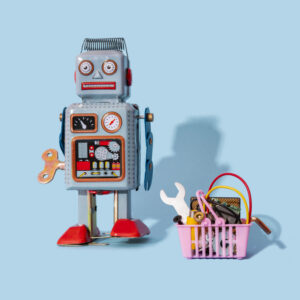 Studio shot of vintage robot toy standing by miniature shopping basket filled with electronic equipment