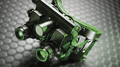 Image of bulky night vision goggles made of black material, but lit with a green light.