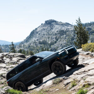 A blue Rivian R1S drives up a 45-degree rock slope.