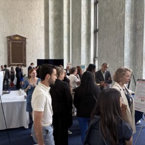 A room full of people standing around a hand full of poster-sized presentations.